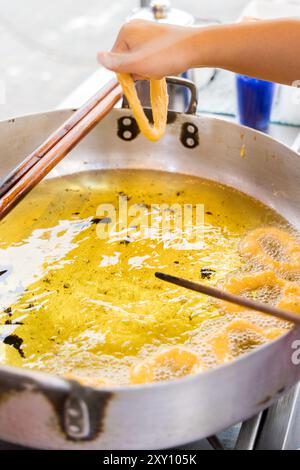 A woman is cooking picarones in a pan. The food is being cooked on a ...