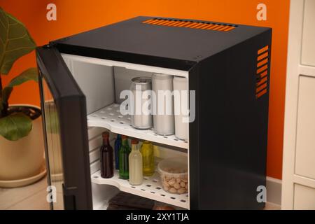 Mini refrigerator with different drinks and snacks near white wall ...