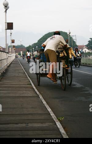 Rear view of a pedicab driver pedaling his trishaw on the old bridge ...