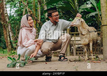 Cheerful Asian couple watching the goat eating leaves in livestock farm ...