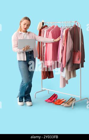 Female stylist with laptop and on rack against blue background Stock ...
