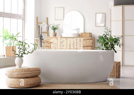 Wicker poufs, houseplant and bathtub in interior of modern bathroom ...