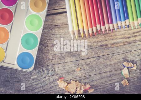 Set of multi-colored pencils, water colors and brushes on a rustically ...