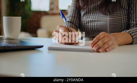 Teleworker at desk transcribing data from laptop to notepad, finalizing ...
