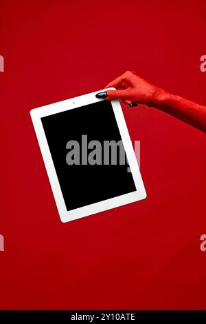 Horror red devil's hand with blank long nails holding tablet with blank ...