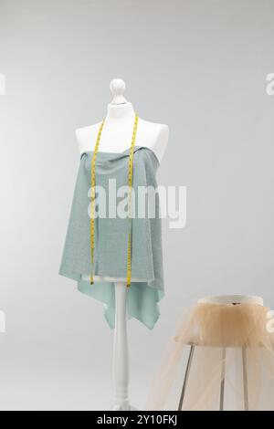 Mannequin with measuring tape, fabric and box on side table against ...
