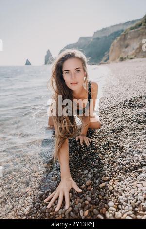 A young woman posing on a pebble beach in a beige swimsuit and open ...