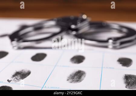 Paper sheet with human fingerprints and handcuffs on table, closeup ...