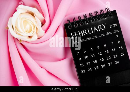 February 2025 desk calendar black color and rose on pink textile ...