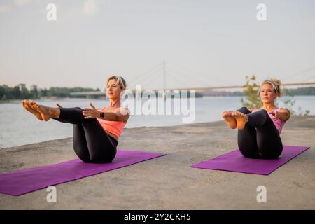 Two women practicing pilates outdoor in the city. Side plank with leg ...