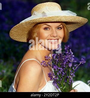 Happy blonde girl wearing a straw hat standing in a vast lavender field ...