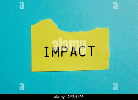 Impact word written on ripped torn yellow paper with blue background ...