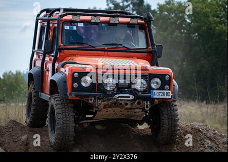 Front view of an orange modified Land Rover Defender jumping over mud ...