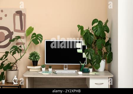 Stylish workplace with computer, books and different houseplants near ...