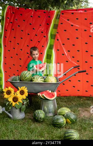 A little boy eats a watermelon. A boy is sitting in a wheelbarrow with ...