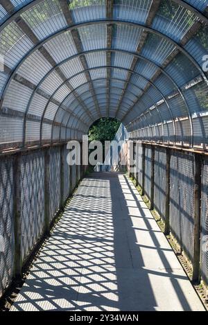Metal cage-like enclosed arched tunnel footbridge over a railway line ...