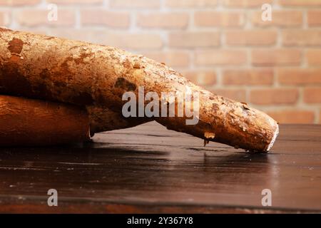 Three cassava roots on a wooden table with a spoon full of tapioca ...