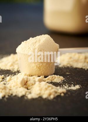 Whey protein powder in a transparent measuring cup with a glass of ...