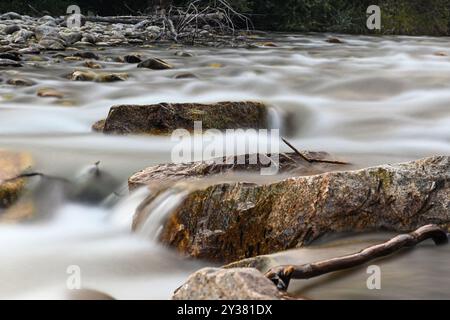Water flows quickly around rocks in a creek, creating a smooth, silky ...