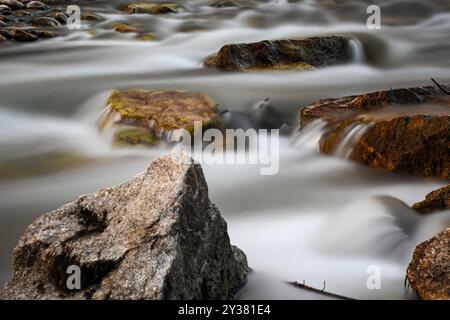 Water flows quickly around rocks in a creek, creating a smooth, silky ...