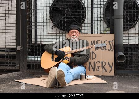 Mature homeless man playing guitar near fence on street Stock Photo - Alamy