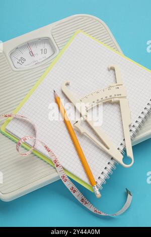 Body fat caliper, measuring tape, scale and notebook on light blue ...