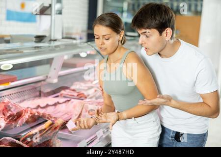 Spouse near butcher shop window inspects goods and choose piece of beef ...
