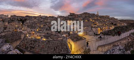 As the sun sets in Matera Italy, a couple holds hands while admiring ...
