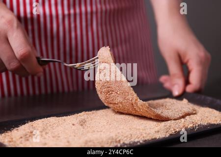 Making schnitzel. Woman coating slice of meat with bread crumbs at dark ...