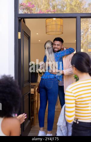 Welcoming friends at door, man hugging woman while another friend ...
