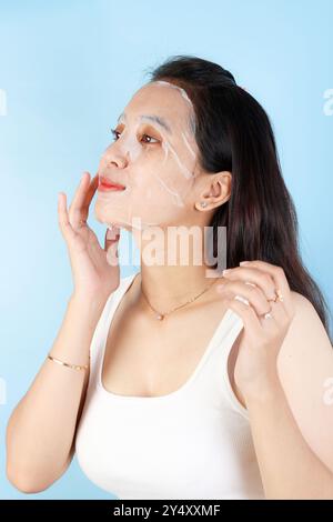 Young woman applying sheet face mask to moisturize skin after shower ...