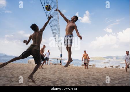 Multinational teams of people play beach volleyball on beach in summer ...