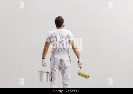 Rear view of painter man looking at white wall, with paint roller and ...