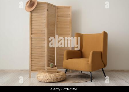 Comfortable armchair with folding screen and ottoman near white wall ...