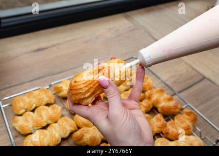 A woman fills eclairs with custard mass using a pastry bag Stock Photo ...