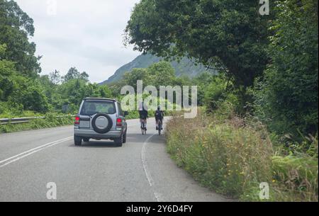 All-terrain vehicle moving slowly behind two cyclists placed side by ...