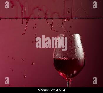 Red wine flows down into a glass. Dark red background with copy space ...