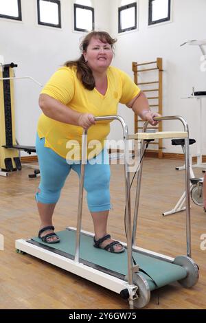 a woman with excess weight is running on a track in the park to lose ...