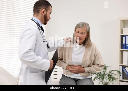 Doctor consulting senior patient with stomach pain at table in clinic ...