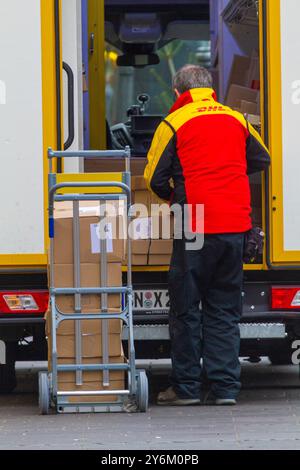 DHL parcel delivery man in uniform working at cycling along road on ...