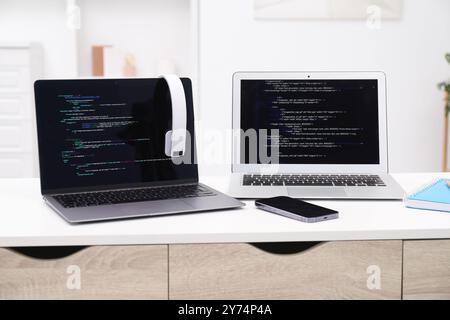 Programmer's workplace. Modern laptops with unfinished code, headphones and smartphone on desk ...