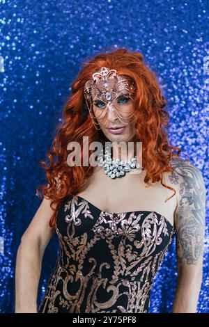 A drag performer in a colorful dress wearing 2 LGBTQ+ flags in his hair ...