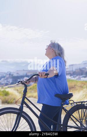 An overweight mature woman rides a black retro-style bicycle against a ...