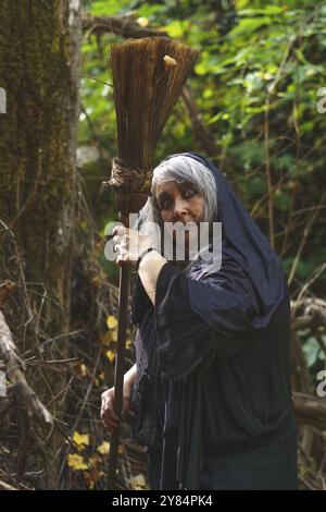 Woman dressed in a black hooded cloak is standing in a darkness next to ...
