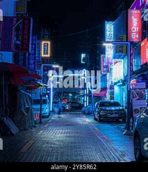 Urban night scene shows a busy street with parked scooters, lighted ...