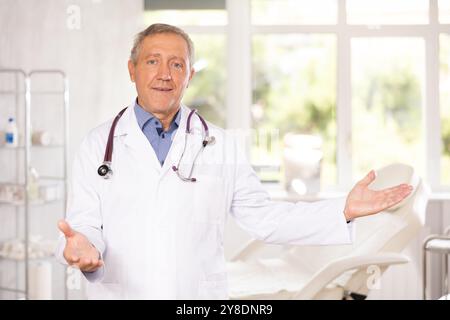 Old man doctor posing in doctor's cabinet with clinical chair Stock ...