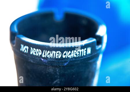 A close-up photo of an ashtray featuring a sign that reads "Just Drop ...