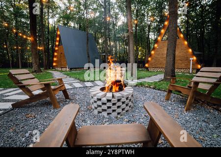 Campfire area with wooden chairs and cabins in background, creating a cozy outdoor gathering ...