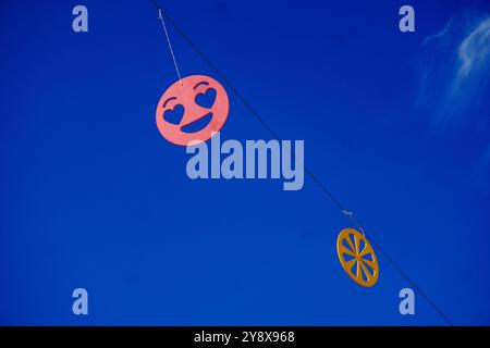 Two suspended objects , a smiling orange emoji against a clear blue sky ...