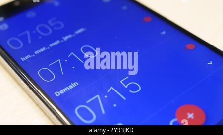 A smartphone displaying multiple alarm times on a wooden surface ...